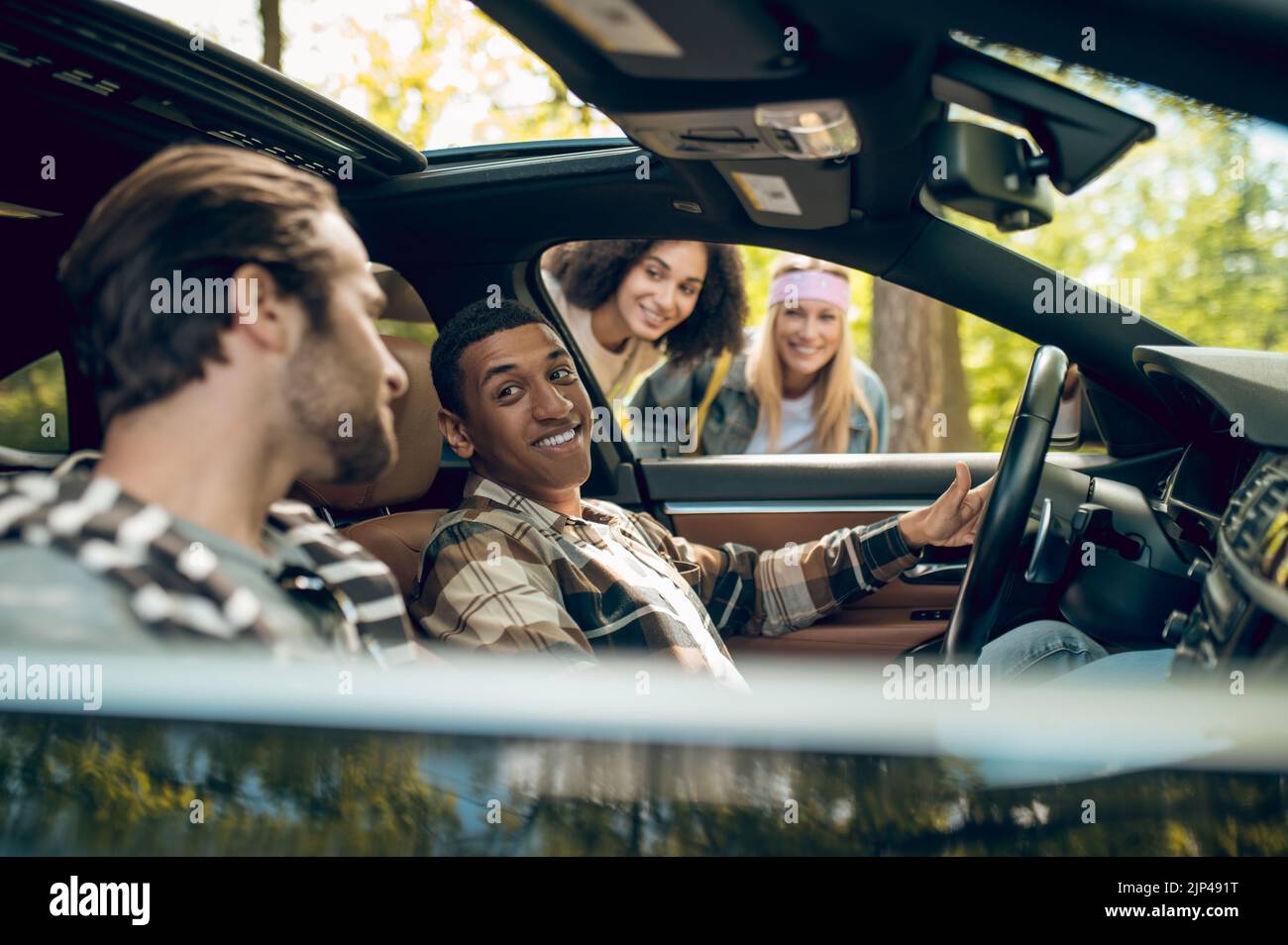 Smiling men in a car talking to girls on the road Stock Photo - Alamy