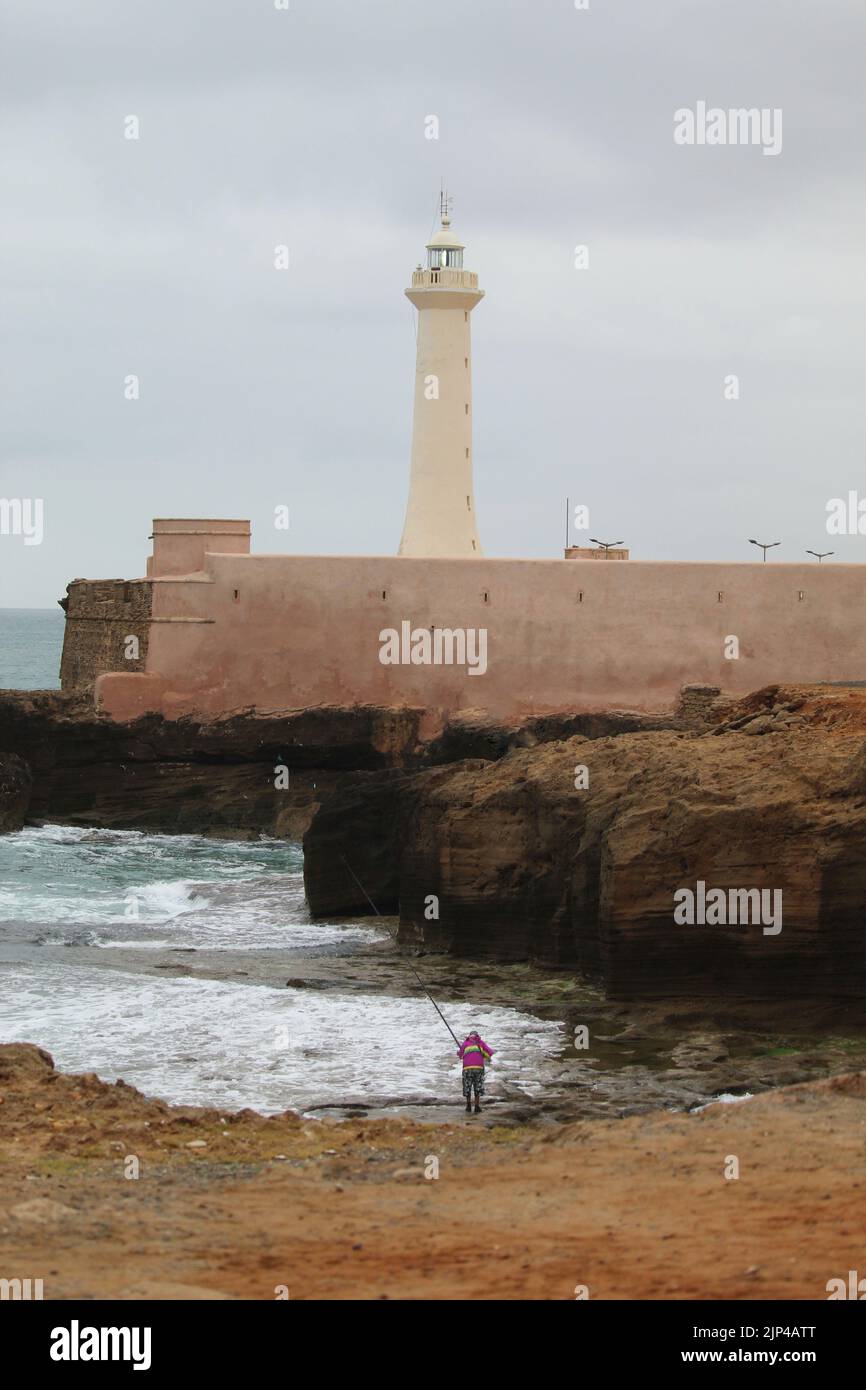 The vertical view of a man fishing by the old lighthouse on a rainy day ...