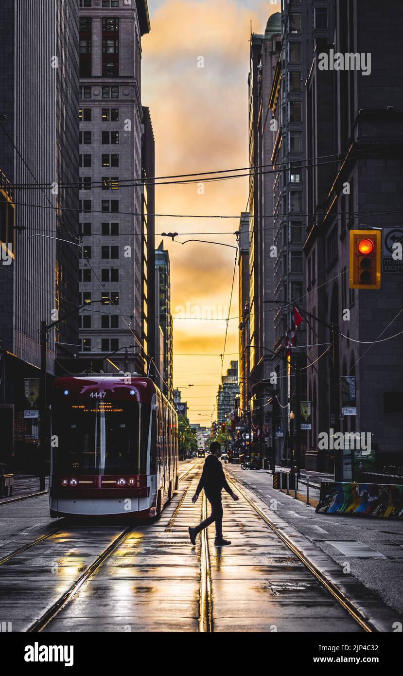 A vertical shot of a man crossing the street in between tall buildings ...
