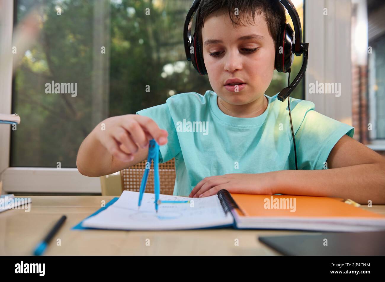Smart schoolboy in audio headset, using a compass to draw a circle in a ...