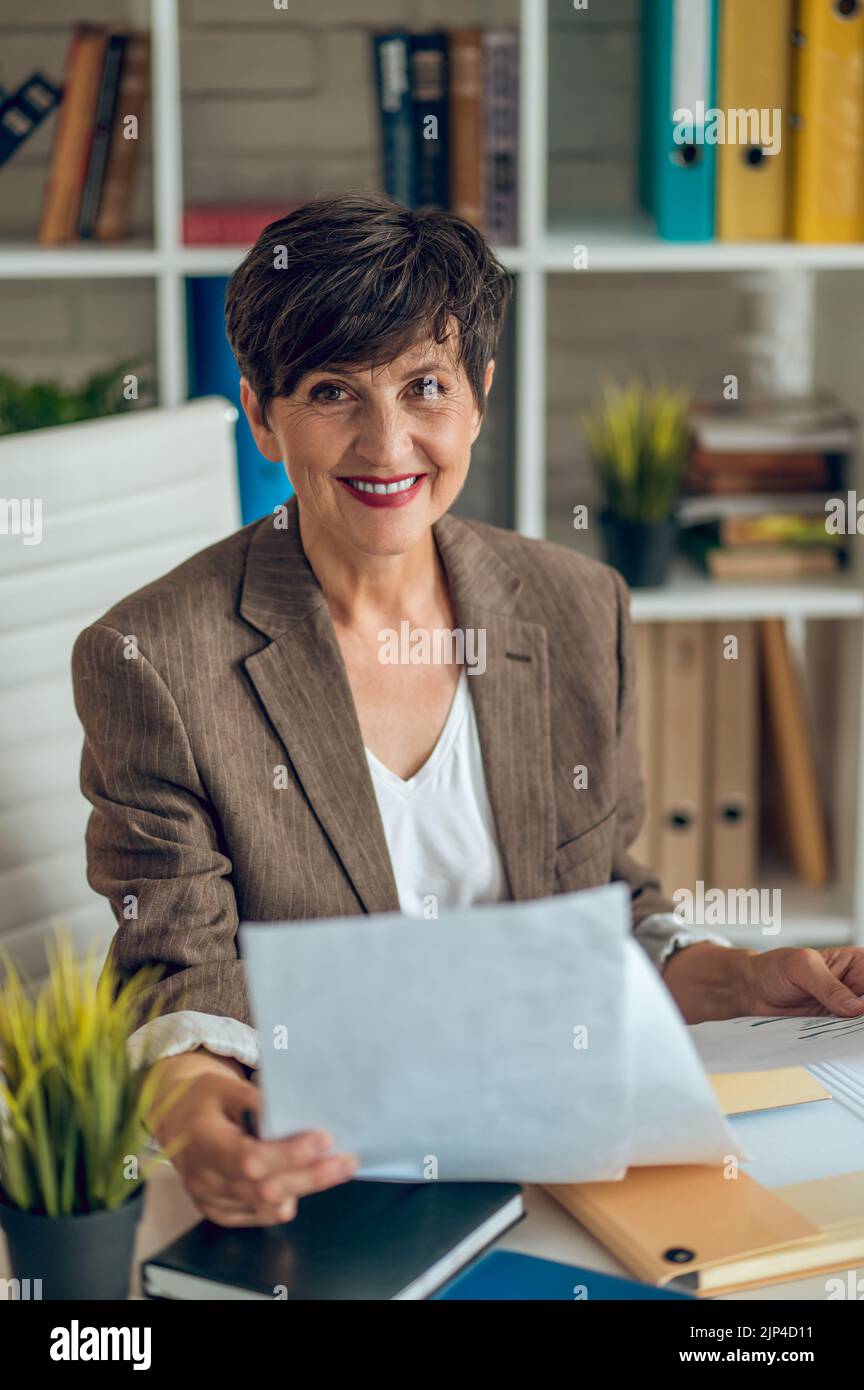 Short-haired mid aged woman sitting at the table in the office and ...