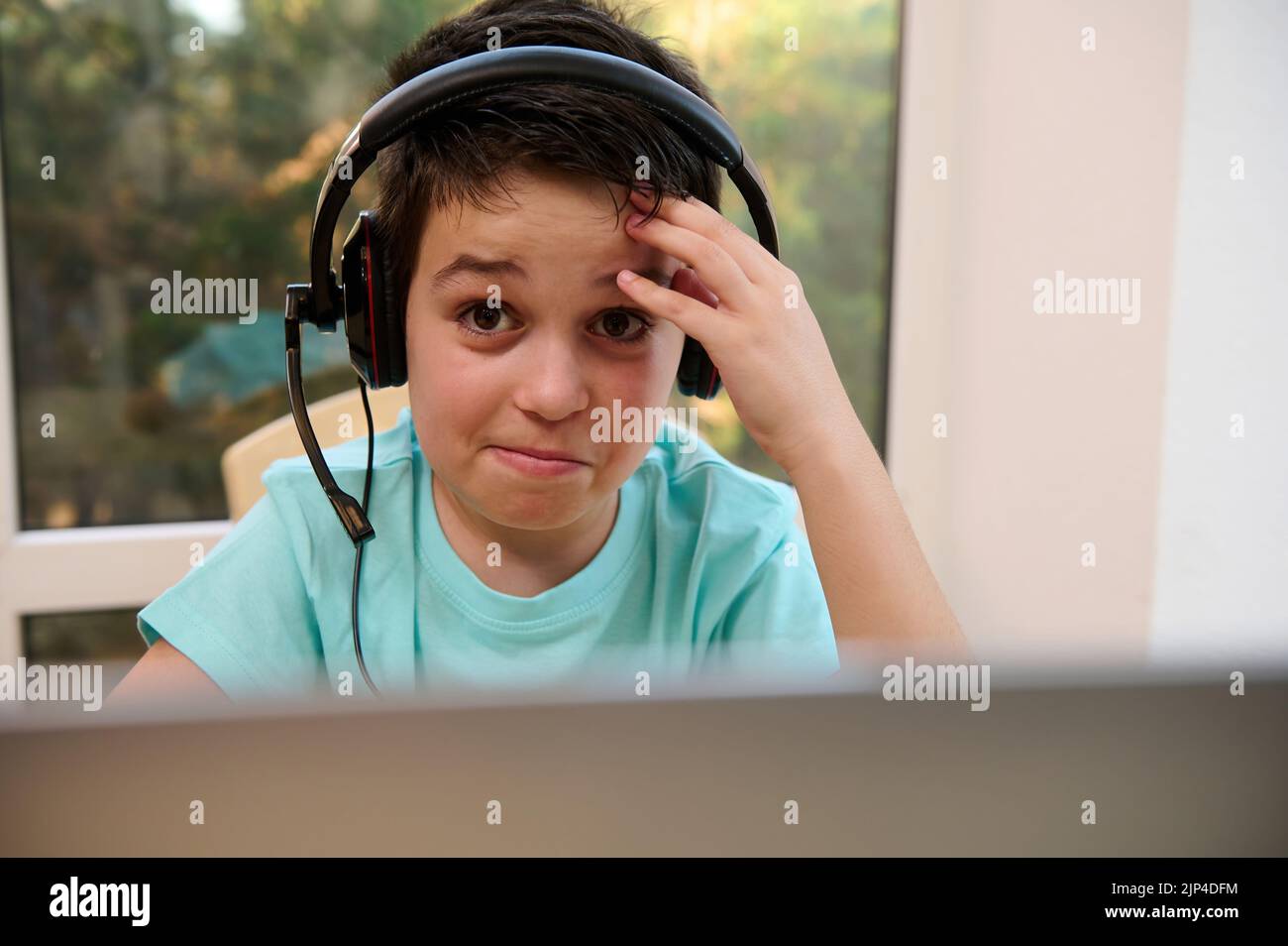 Smart schoolchild in audio headset, smiles cutely looking at camera ...
