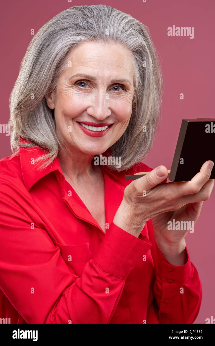 Mature woman in red doing makeup and looking contented Stock Photo - Alamy