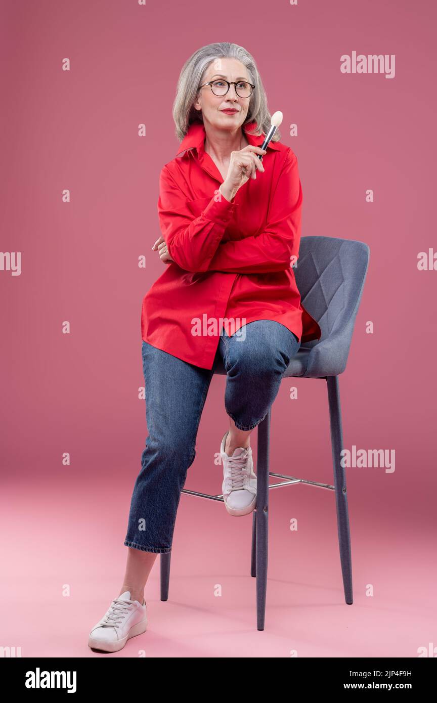 Good-looking mid aged woman in a studio holding a face brush in hand ...