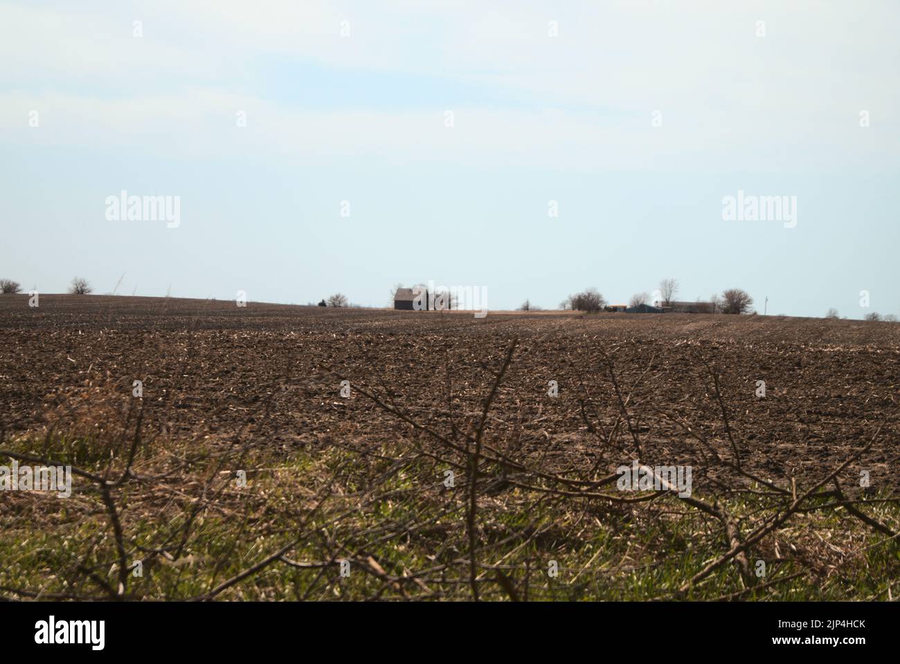 A vast unplanted corn field with a few small wooden houses under a ...