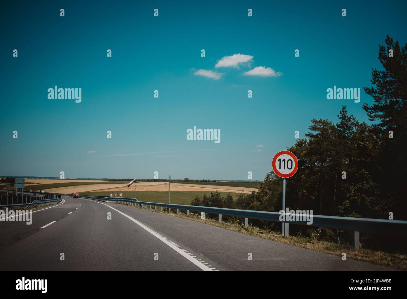 An oval speed restriction sign near an empty highway road with railings ...