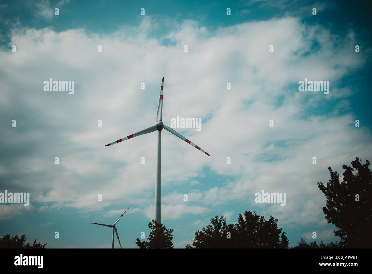 A closeup shot of a wind turbine on a wind power plant with trees under ...