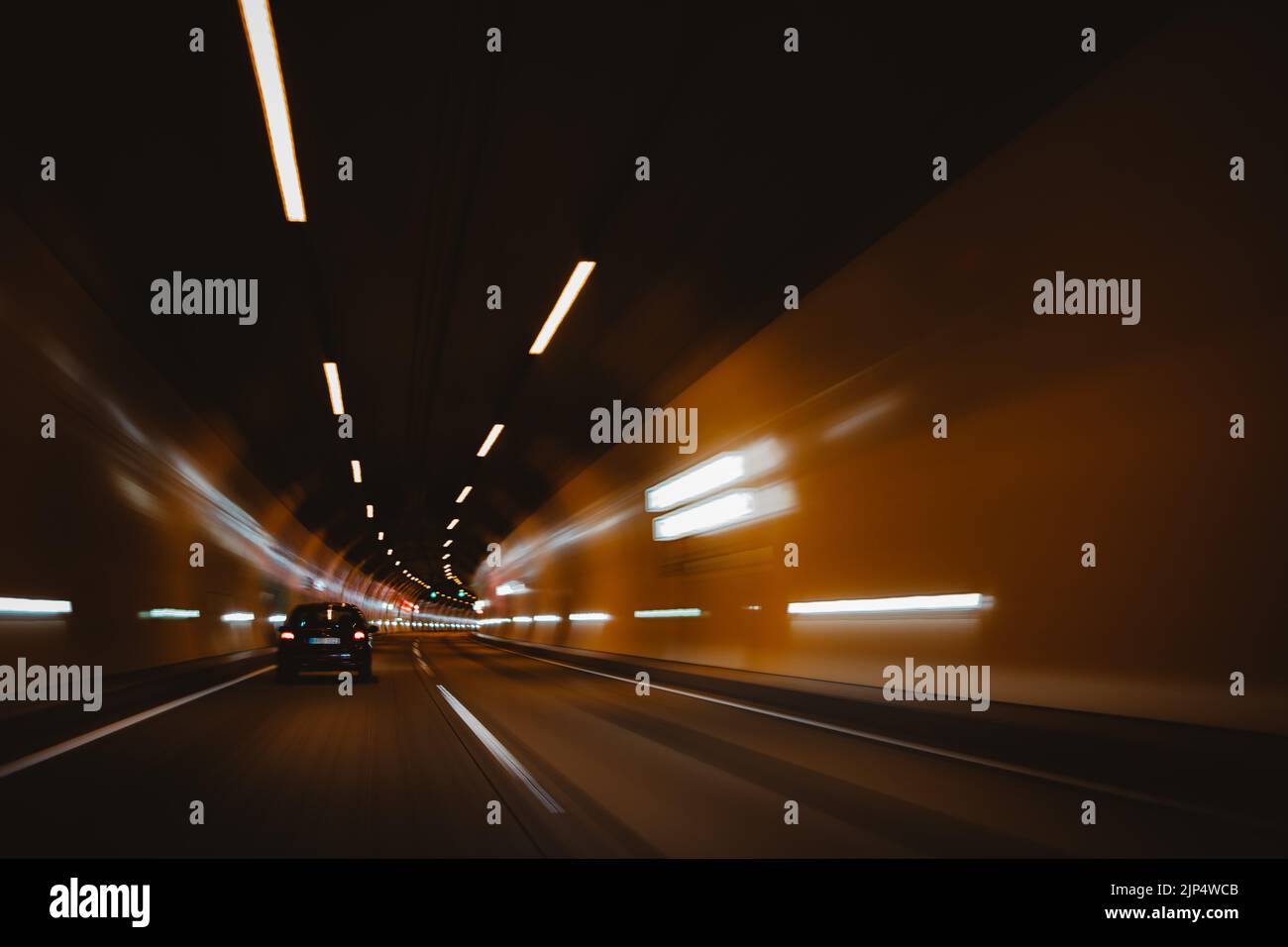 A blurred shot of a black car driving fast in a tunnel with lights on ...