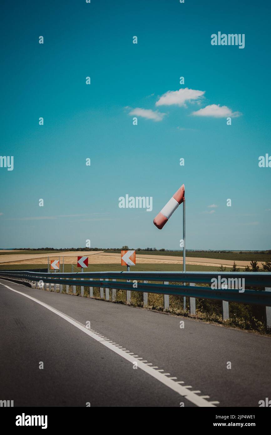 A vertical shot of a windsock and road signs near the railing of an ...