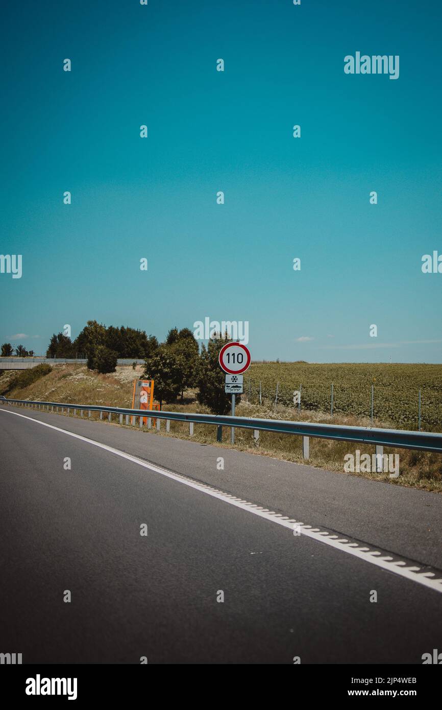 A vertical shot of a railing and a circular warning sign near a road ...