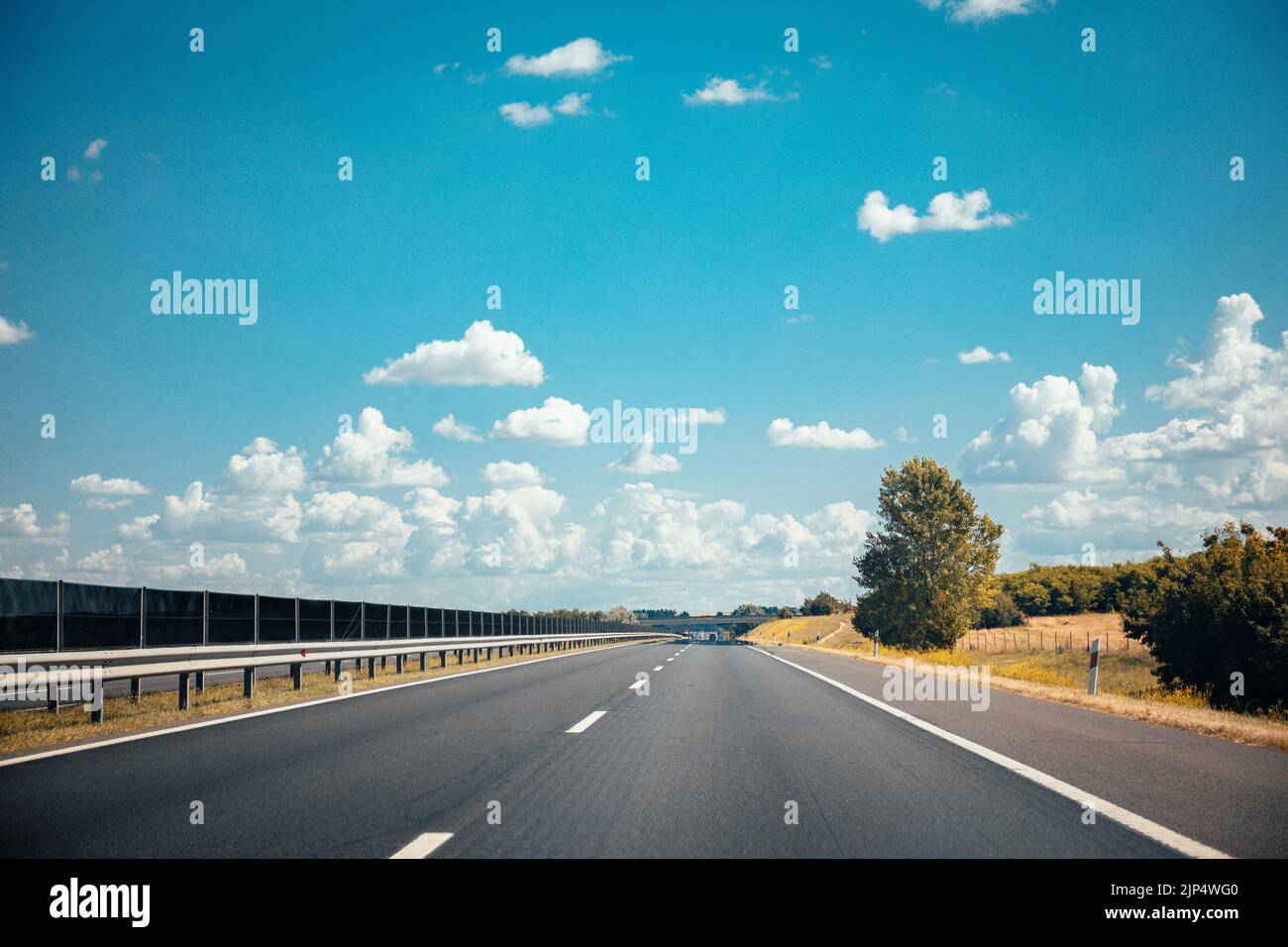 An empty asphalted highway road with white markings, railings, and ...