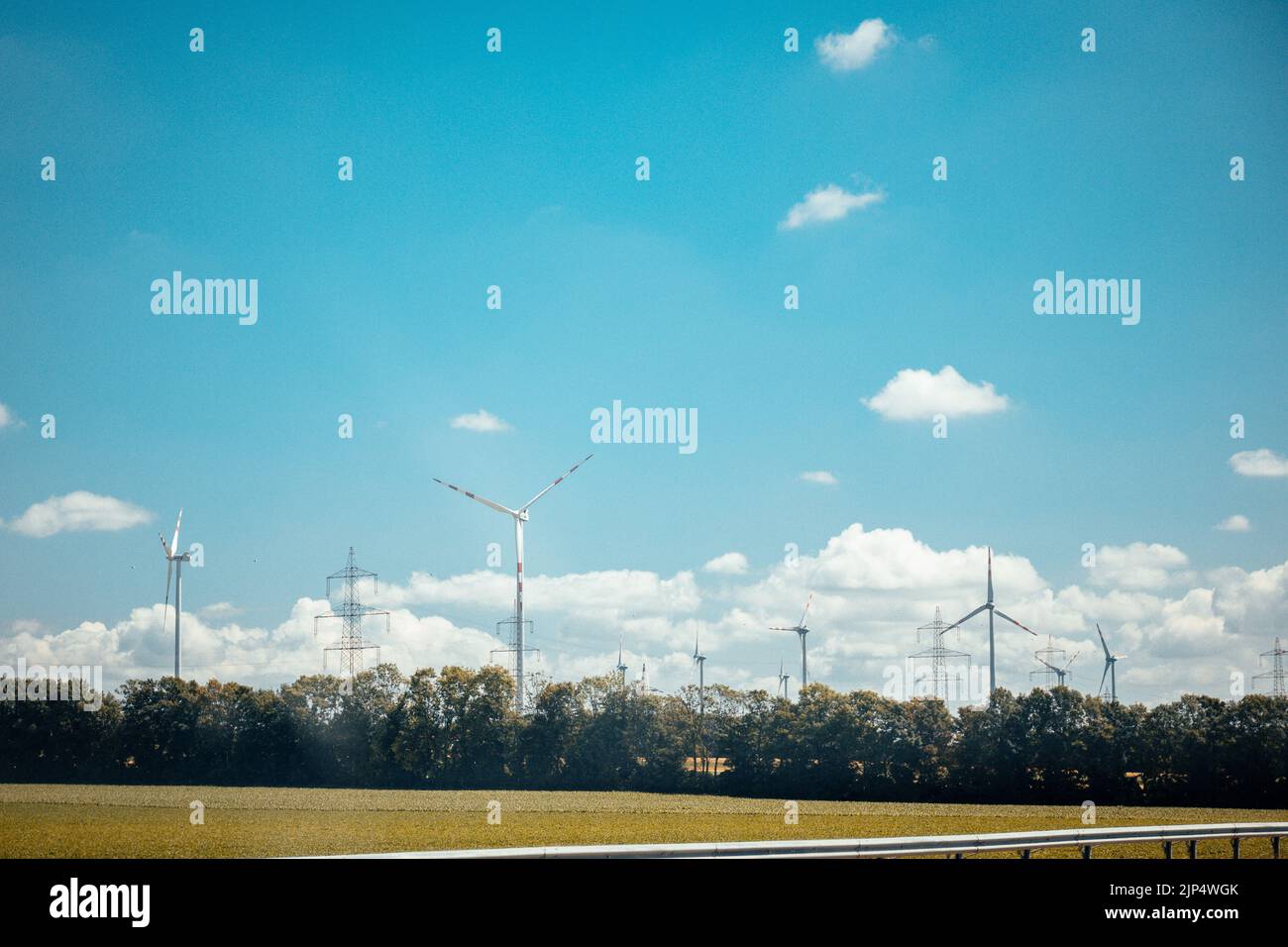 A wind power plant with modern wind turbines and trees under a blue sky ...