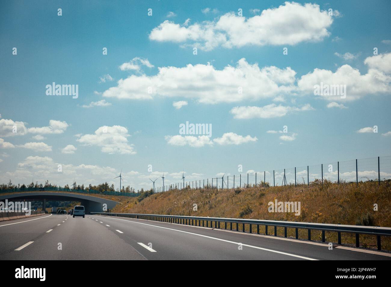 An asphalted road with white markings, cars, railings and a fence ...