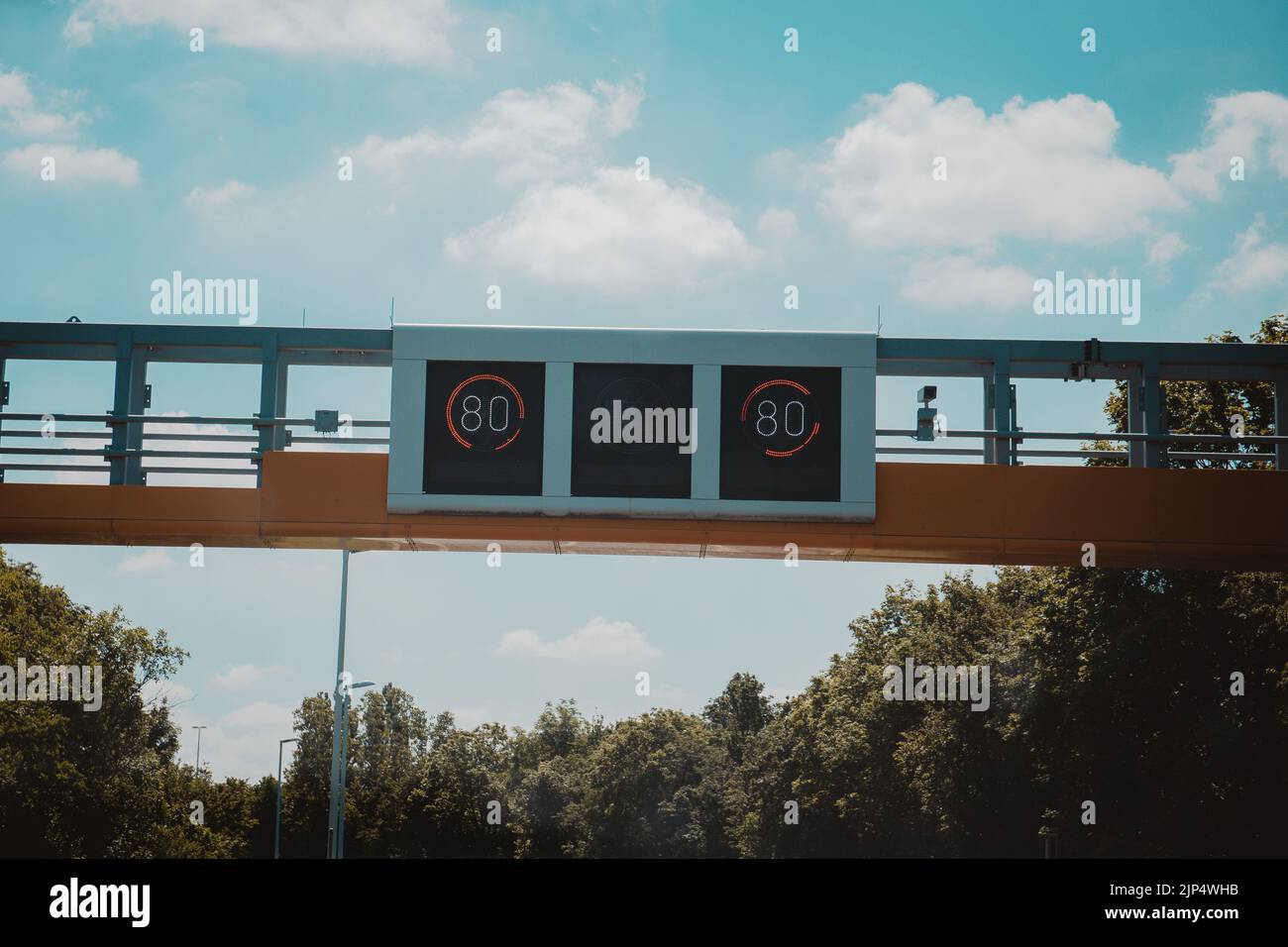 A speed limit road sign over a road surrounded by green trees under a ...