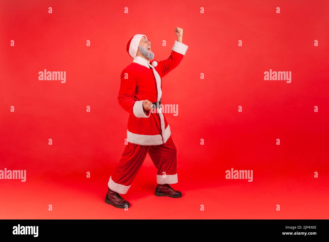 Full length portrait of elderly man with gray beard wearing santa claus costume screaming for ...