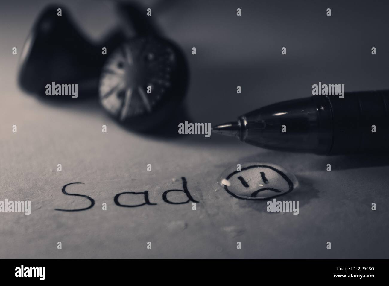 A grayscale depressing shot of a paper with the word sad and a drawn ...