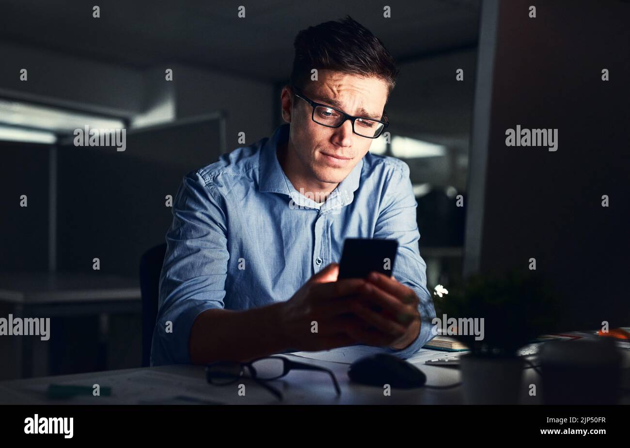 Confused businessman texting on his phone at the office at night ...