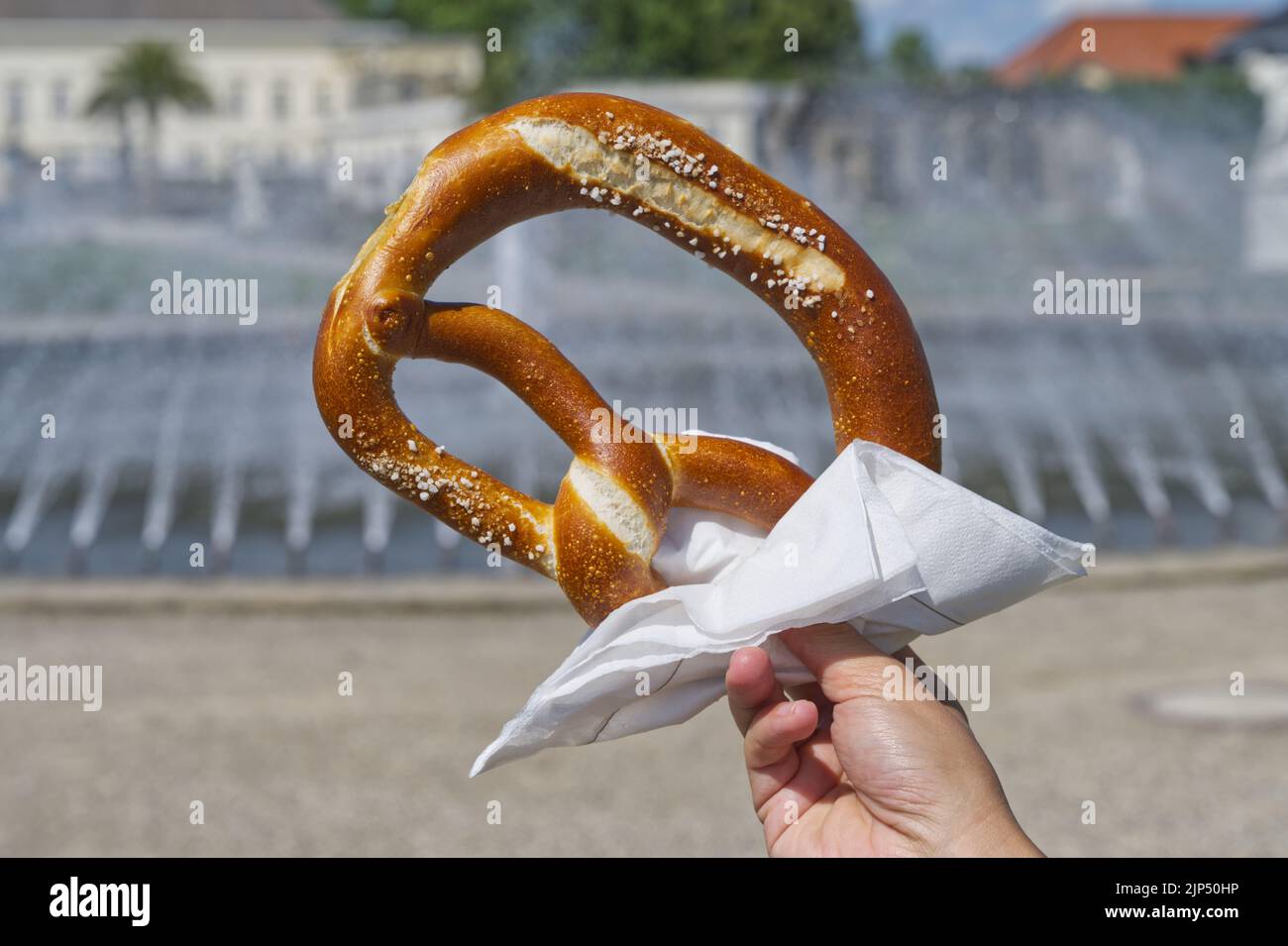 Pretzel in hand typical food in garden in front of fountain in Germany ...