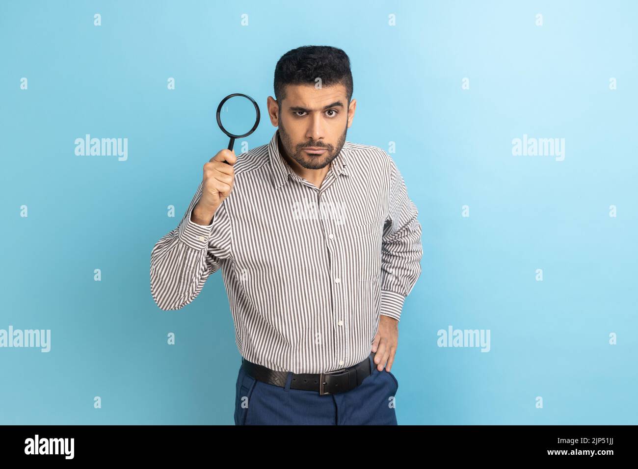 Serious man with beard looking at camera and holding magnifying glass ...