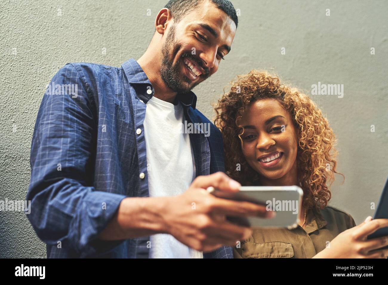 Smiling young couple looking, laughing and holding phone together ...