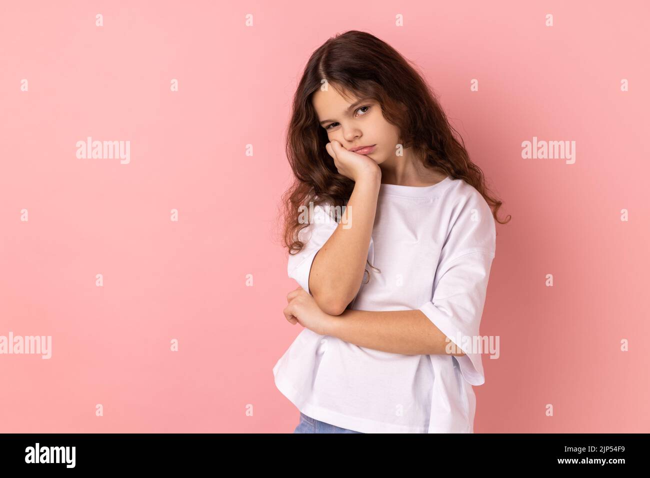 Portrait of lazy bored little girl wearing white T-shirt leaning on ...