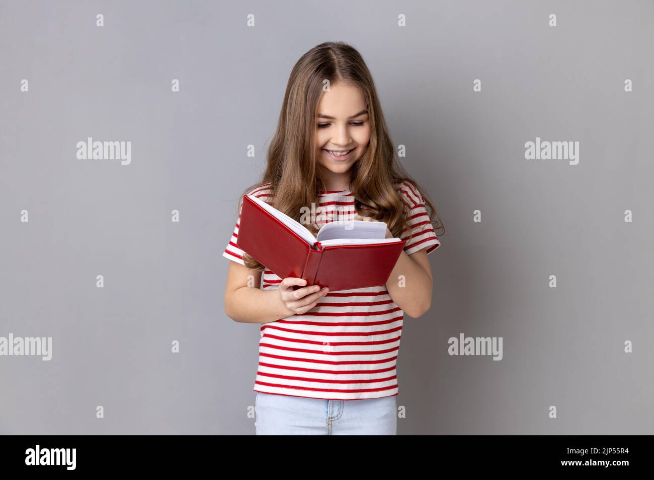 Portrait of smiling satisfied little girl wearing striped T-shirt holds ...