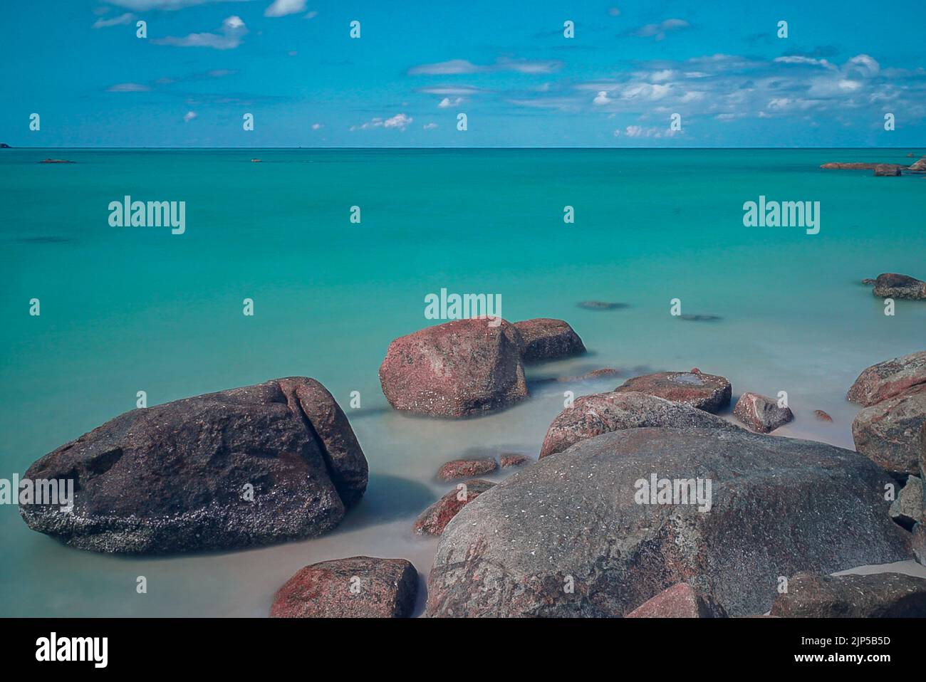 A beautiful shot of calm clear ocean water coast with big rocks on the ...