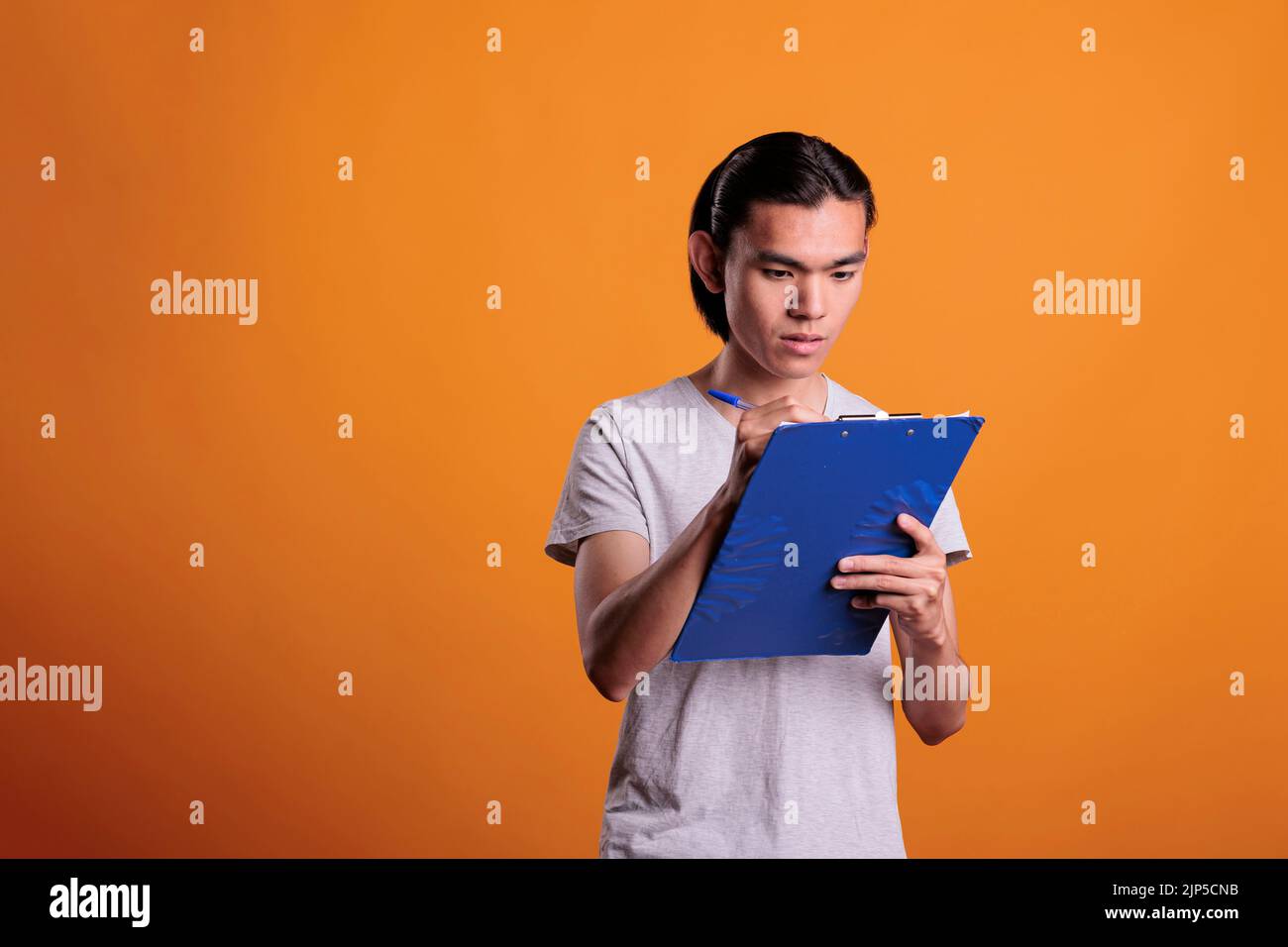 Young asian man taking notes in clipboard, serious student writing in ...