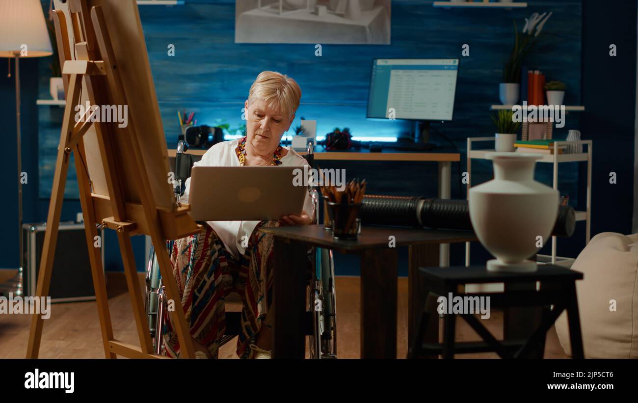 Senior artist with impairment finding inspiration on laptop to draw ...