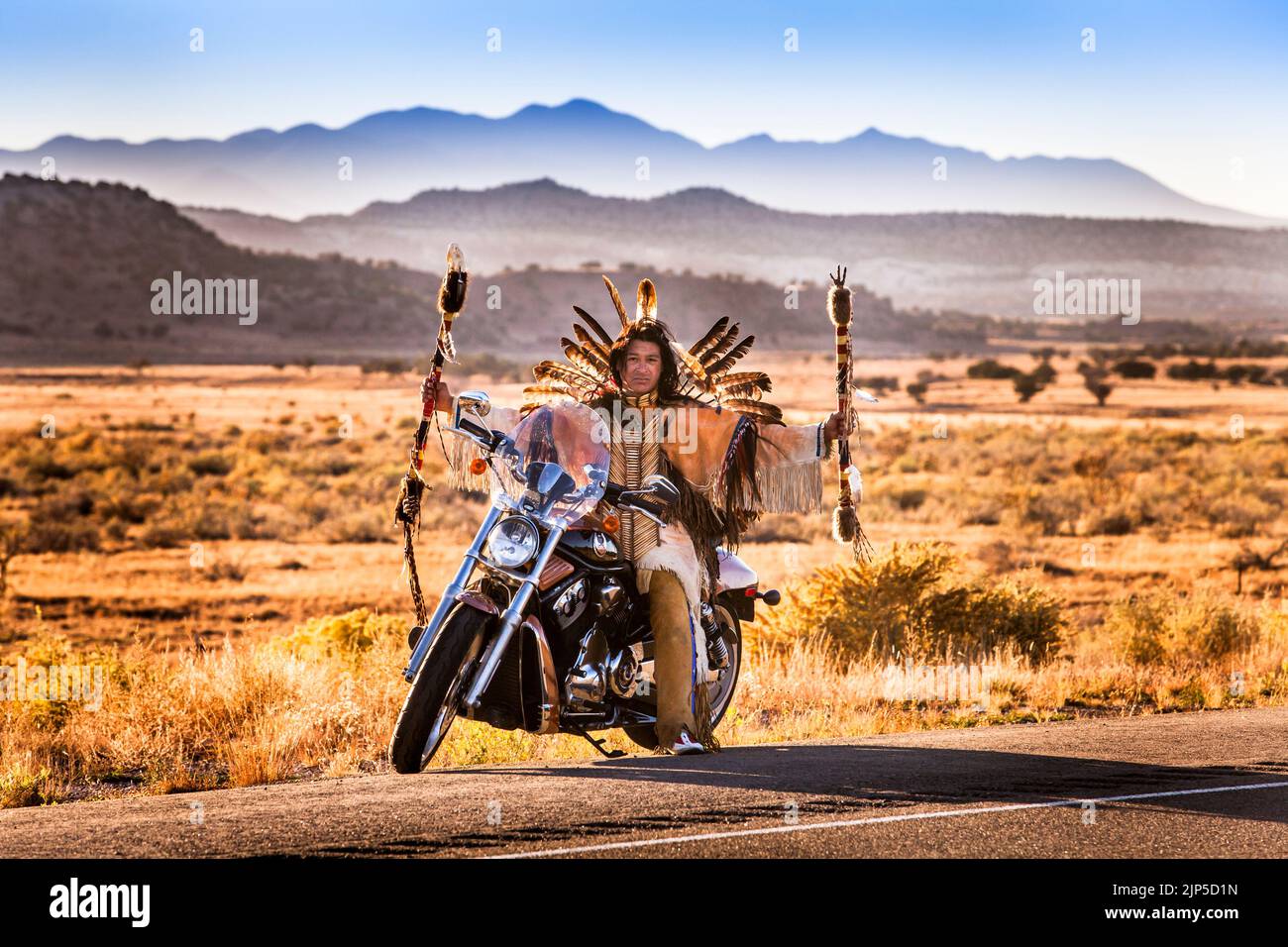 Traditionally dressed Native American man holds up two coup sticks ...