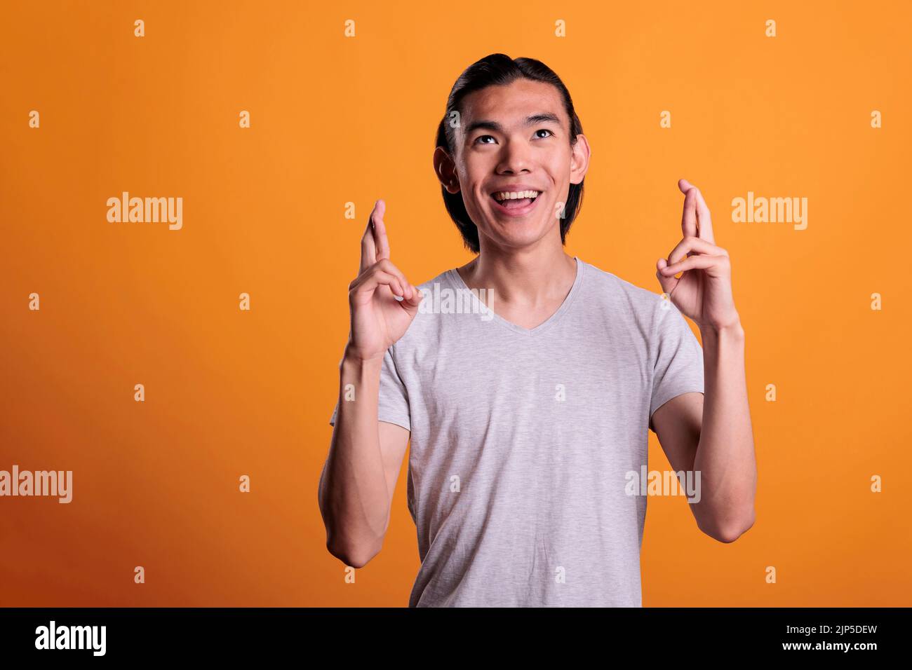 Young asian man crossing fingers, praying for luck, looking upwards ...
