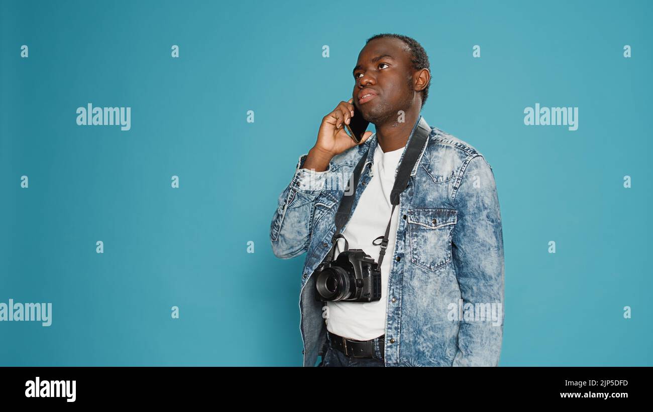 Young photographer talking on mobile phone call over blue background ...