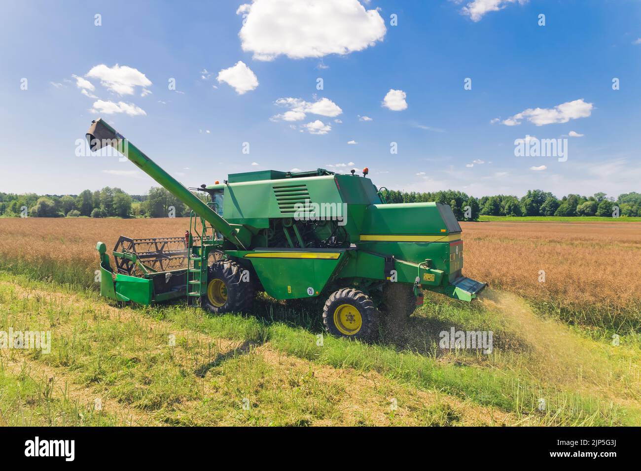 Aerial side view of a green agricultural combine harvester with a ...