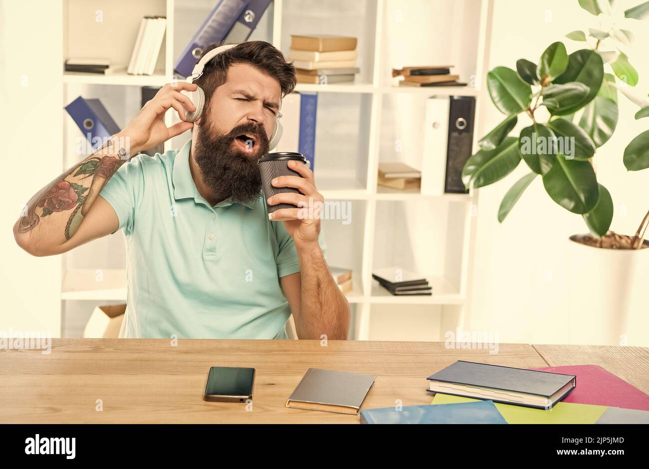 Happy man singing to takeaway cup listening to song in headphones in ...