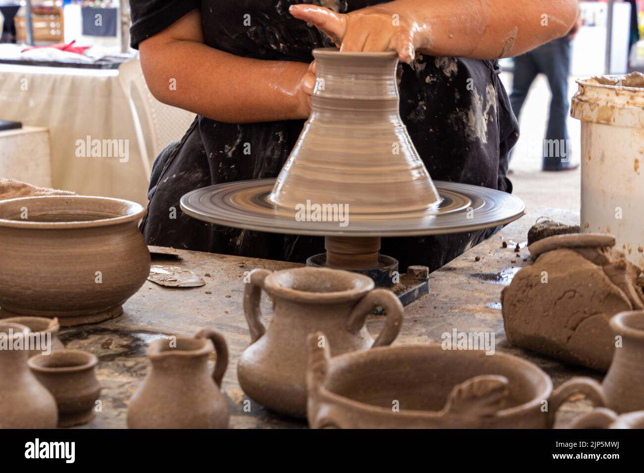 A potter man working on a potter's wheel making a ceramic pot out of ...