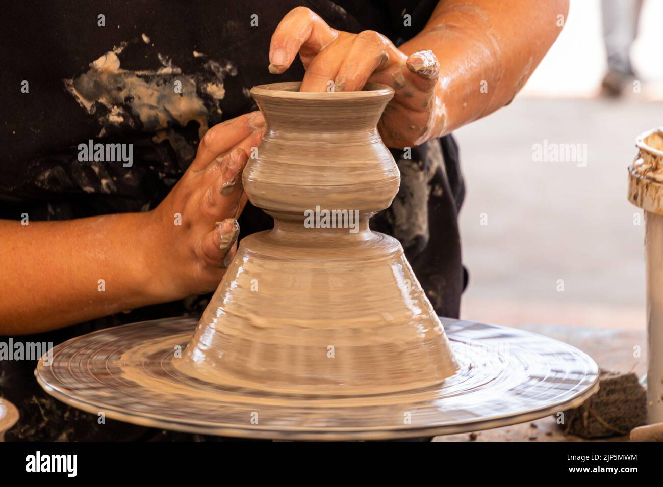 Hands of a potter man working on a potter's wheel making a ceramic pot ...