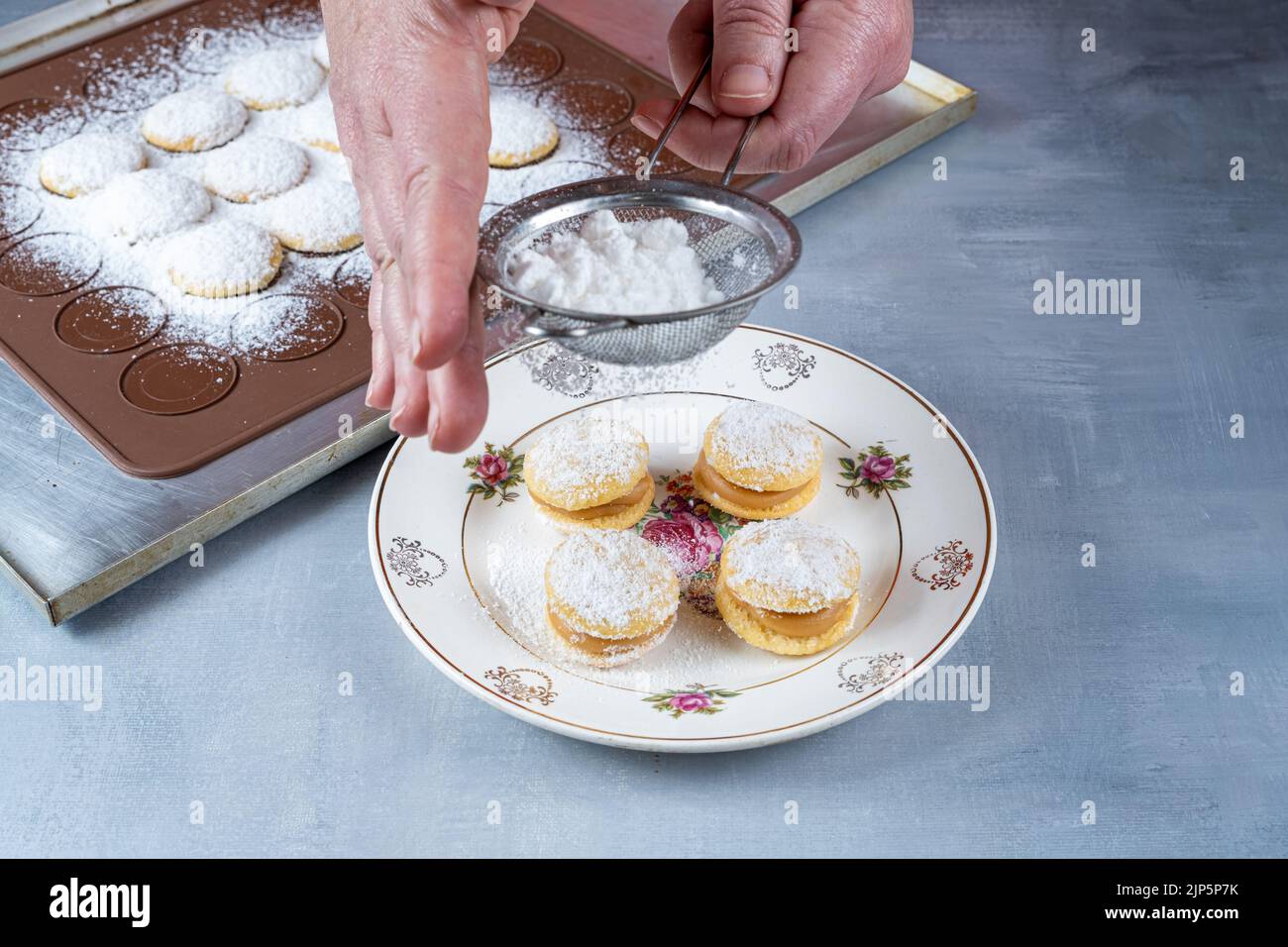 Confectioner using a steel sieve to sprinkle sugar on wedding sweet ...