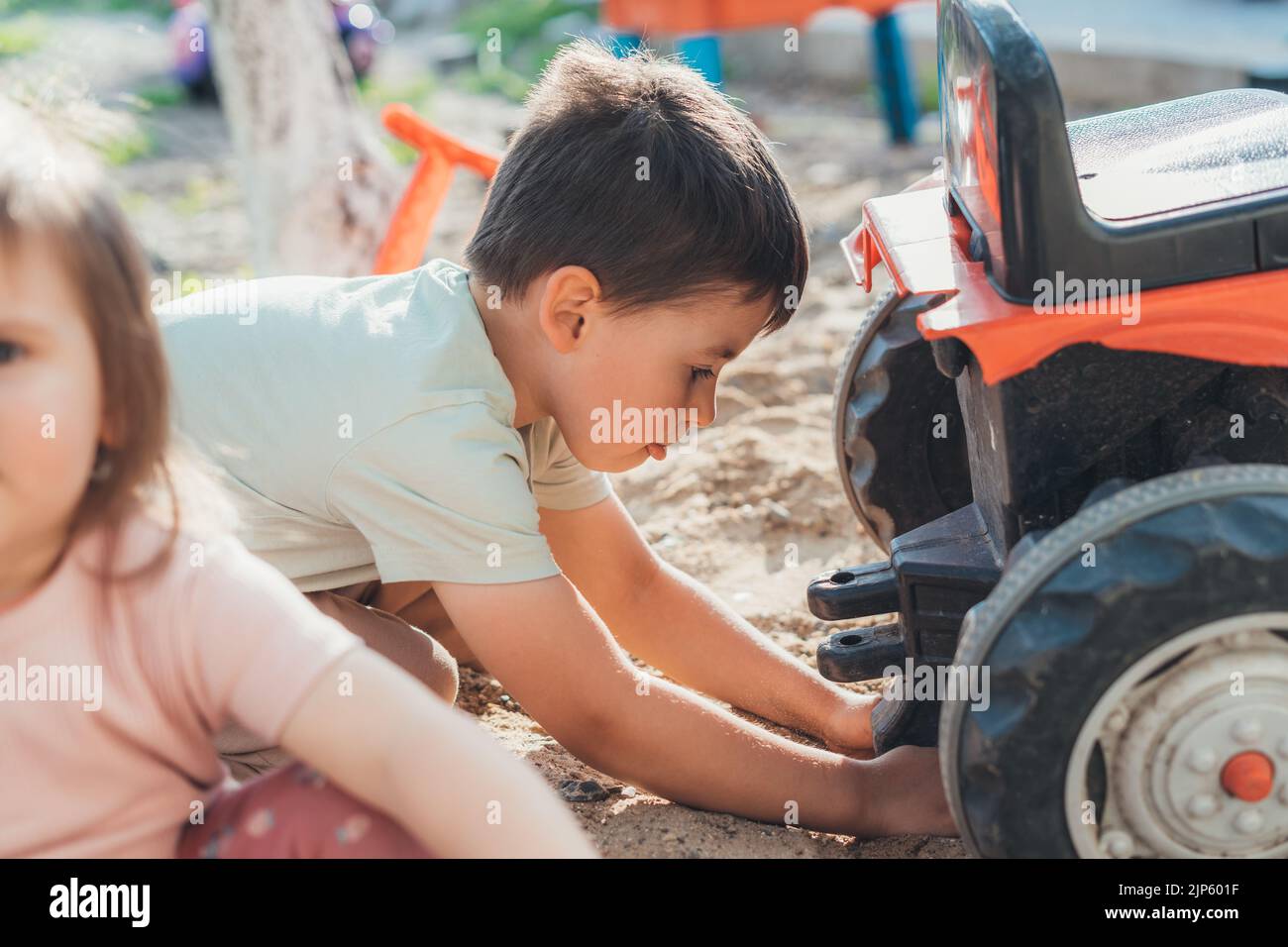 Boy fixing something on his toy car outside in the backyard with his ...