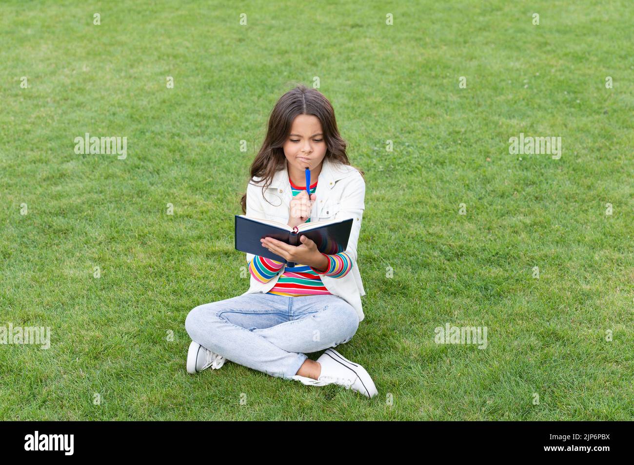 thinking teen child making notes in notebook sitting on grass. taking ...