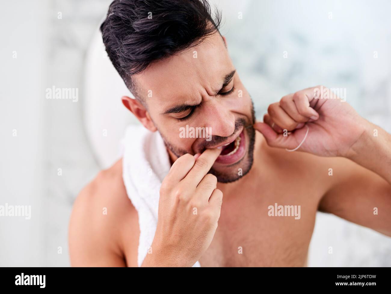 Be careful not to floss too vigorously to prevent dental damage. a handsome young man flossing ...
