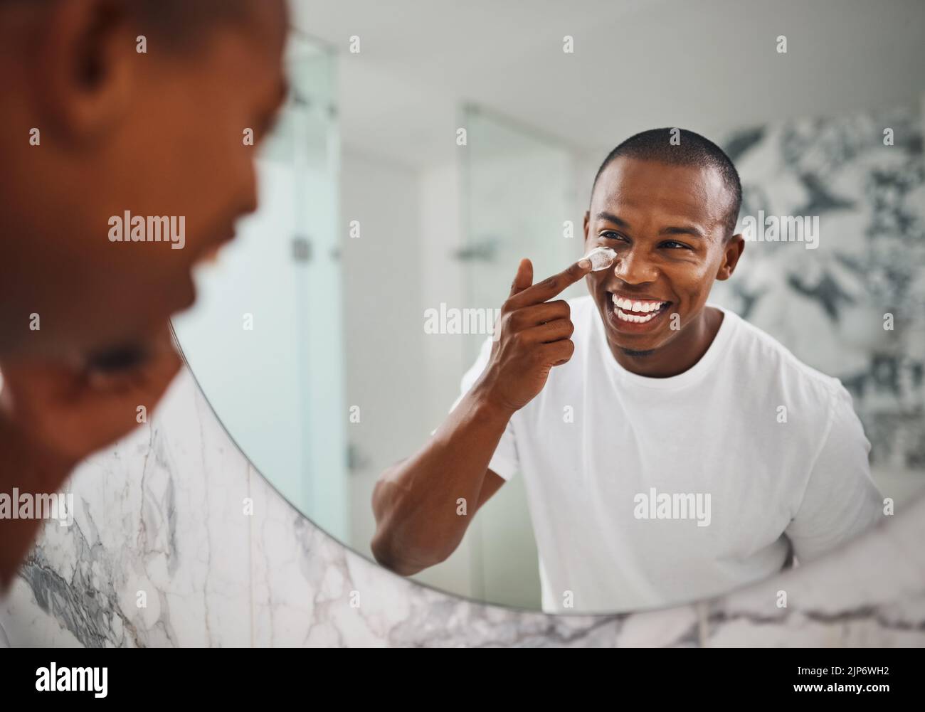 Taking his skincare routine to the next level. a handsome young man applying moisturizer to his ...