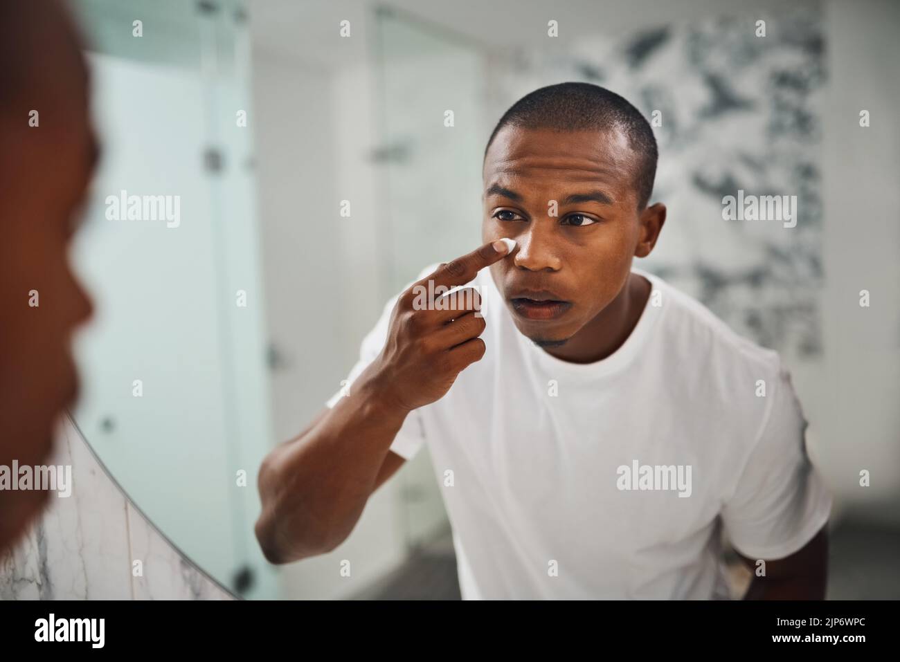 Upping his skincare game. a handsome young man applying moisturizer to his face in the bathroom ...