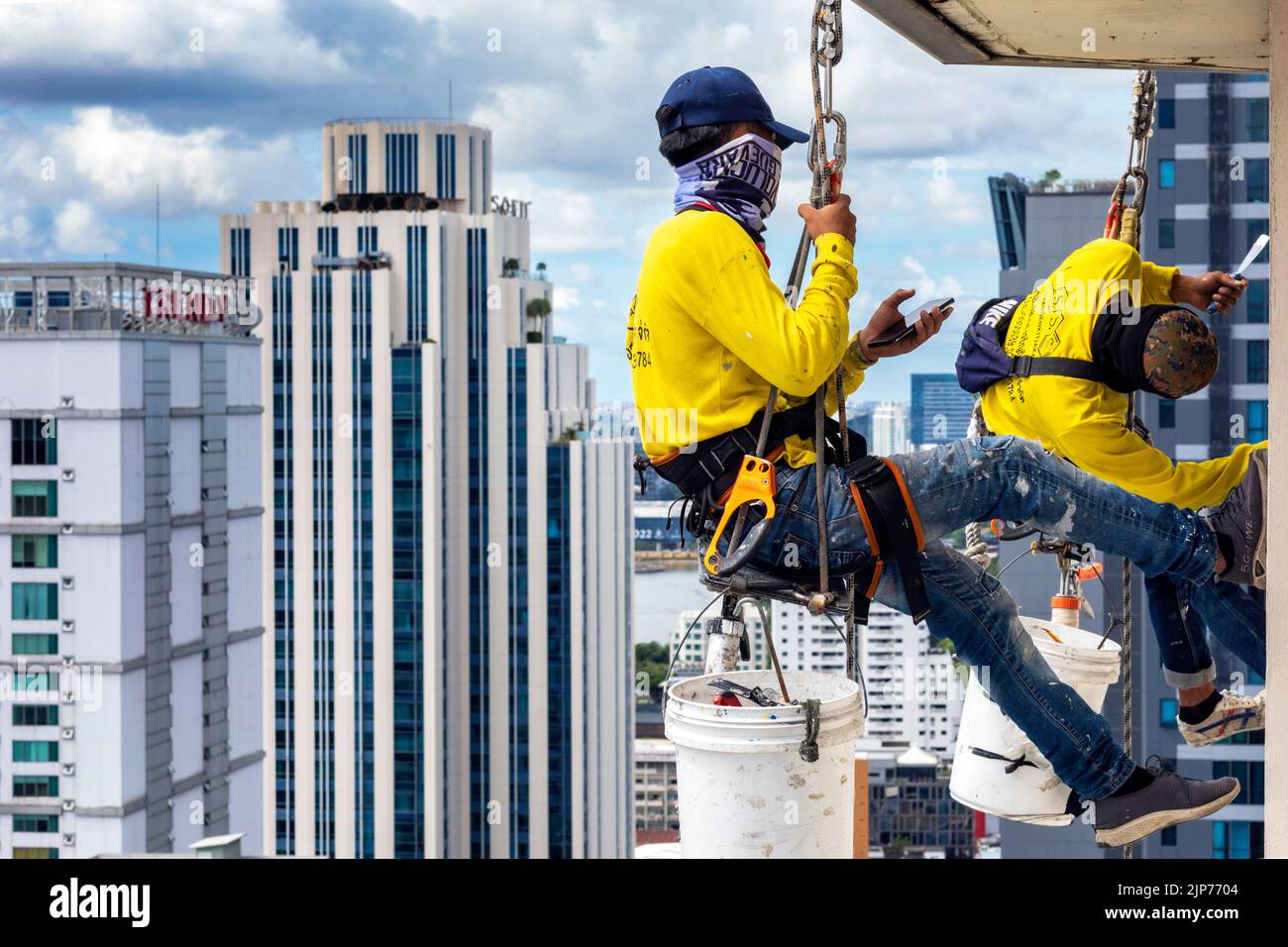 Thai workers repairing windows on high rise skyscraper above Bangkok ...