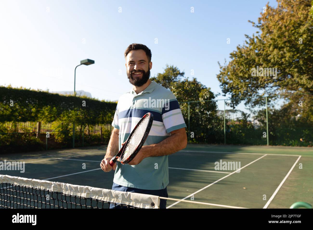 Portrait of happy caucasian man playing tennis standing by net on ...