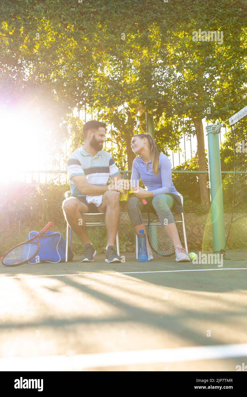 Happy caucasian couple playing tennis sitting on chairs talking at the ...