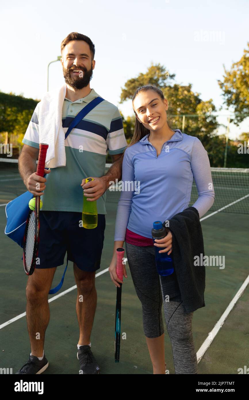 Portrait Of Happy Caucasian Couple Holding Rackets And Water Bottles On