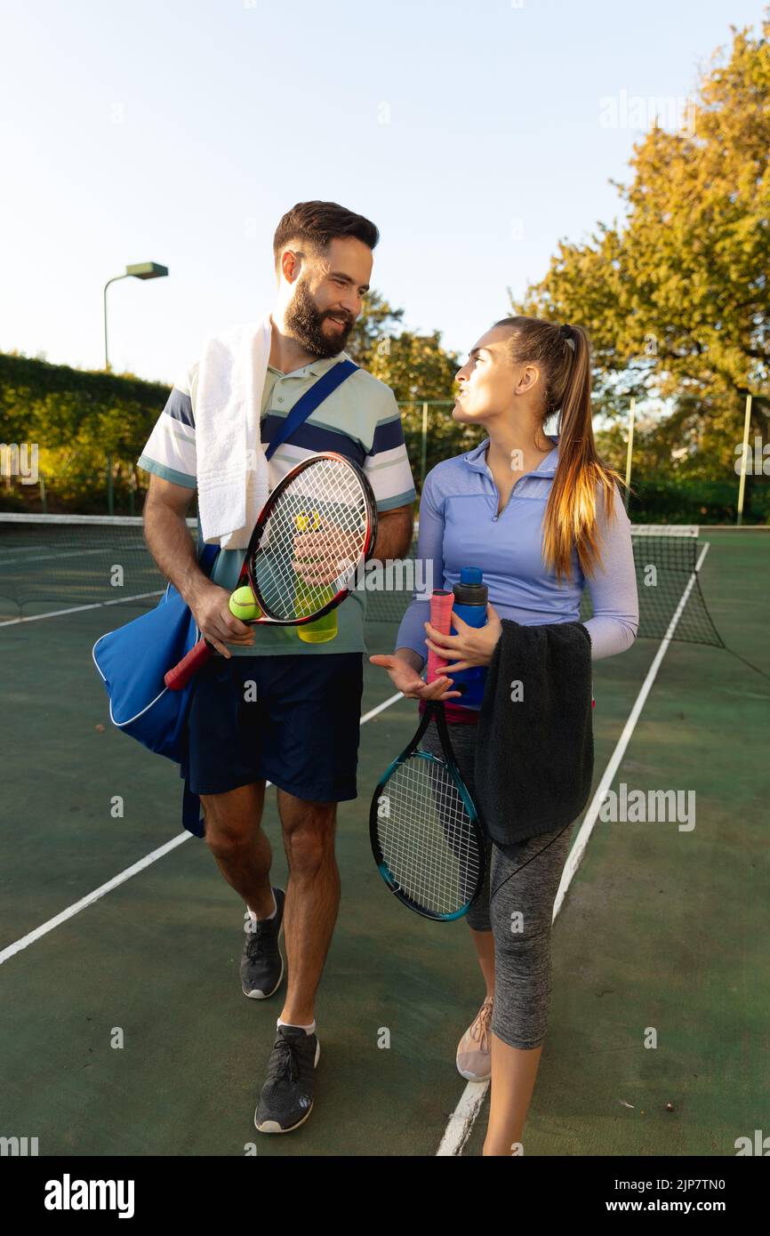 Happy caucasian couple holding rackets and water bottles talking on ...