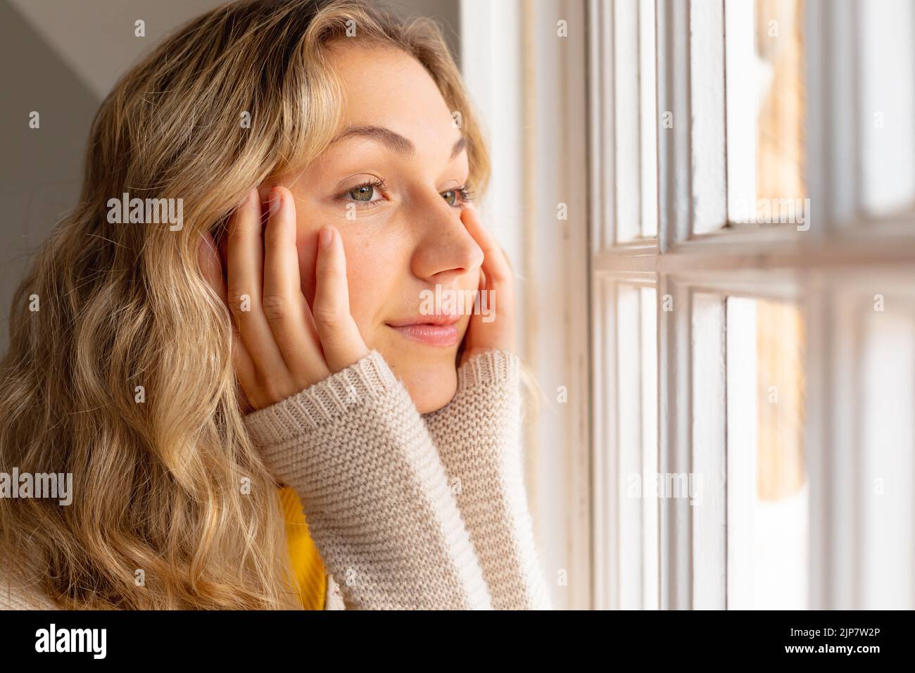 Happy caucasian woman wearing sweater, looking through window and ...