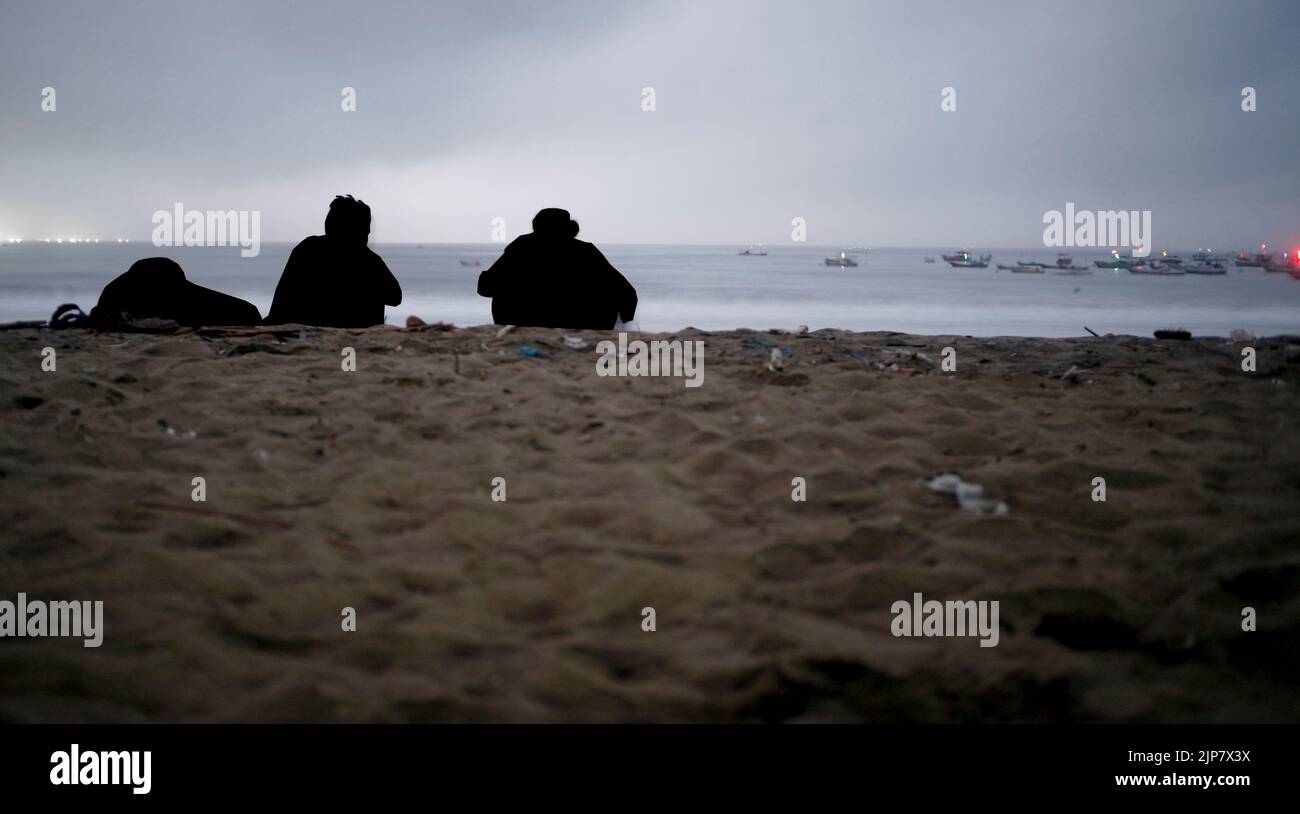 Silhouette of young man siting on the beach looking out to sea at dawn ...