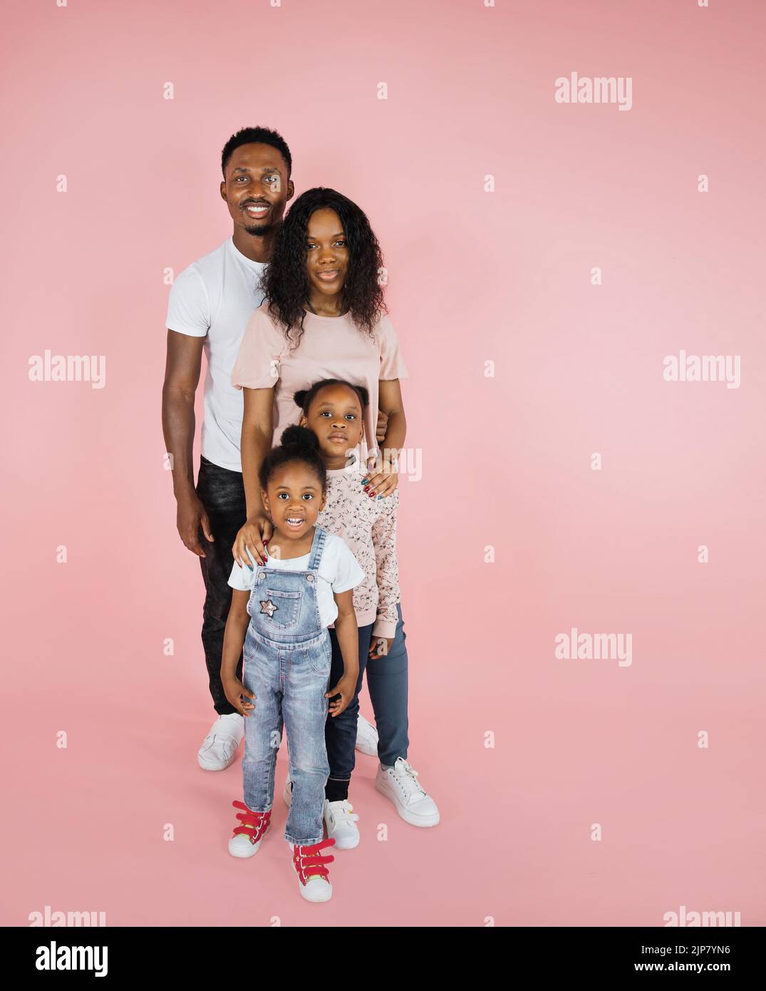 Cheerful african american family of four, standing one behind other and smiling at camera on ...